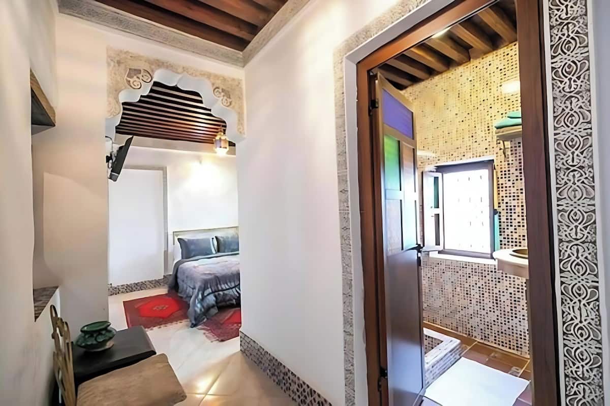 Quarto com cama, mesa de cabeceira e tapete vermelho.