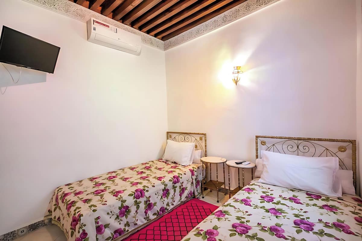 Quarto com duas camas, uma televisão, ar condicionado e uma mesinha de cabeceira com abajur.