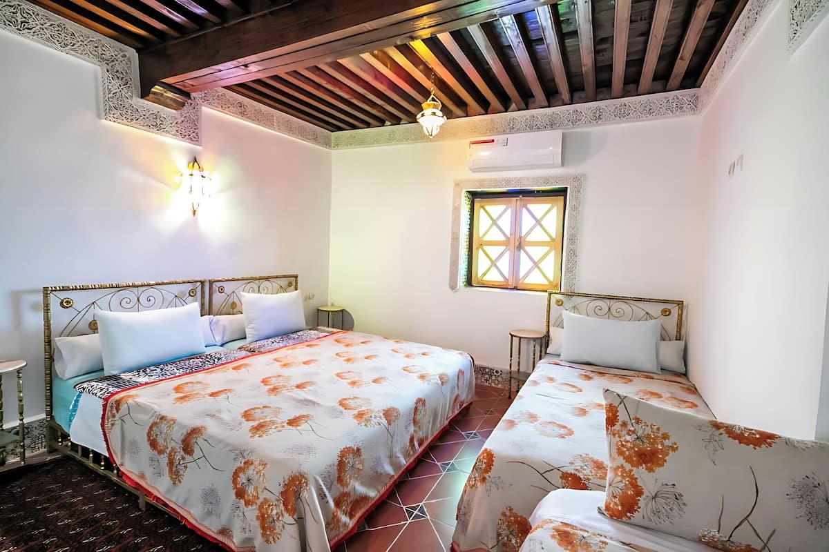 Quarto com duas camas, uma janela com moldura decorativa e teto com vigas aparentes.