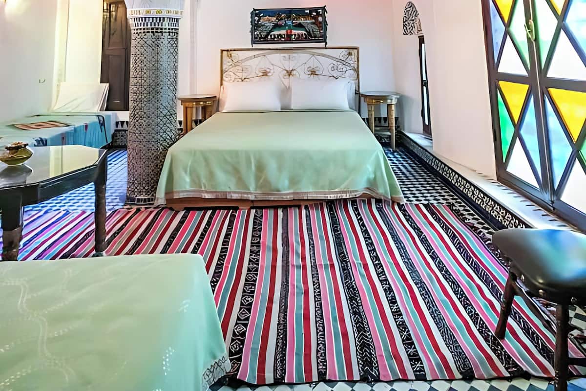 Um quarto com uma cama, uma cadeira, uma mesa e um pilar decorativo.