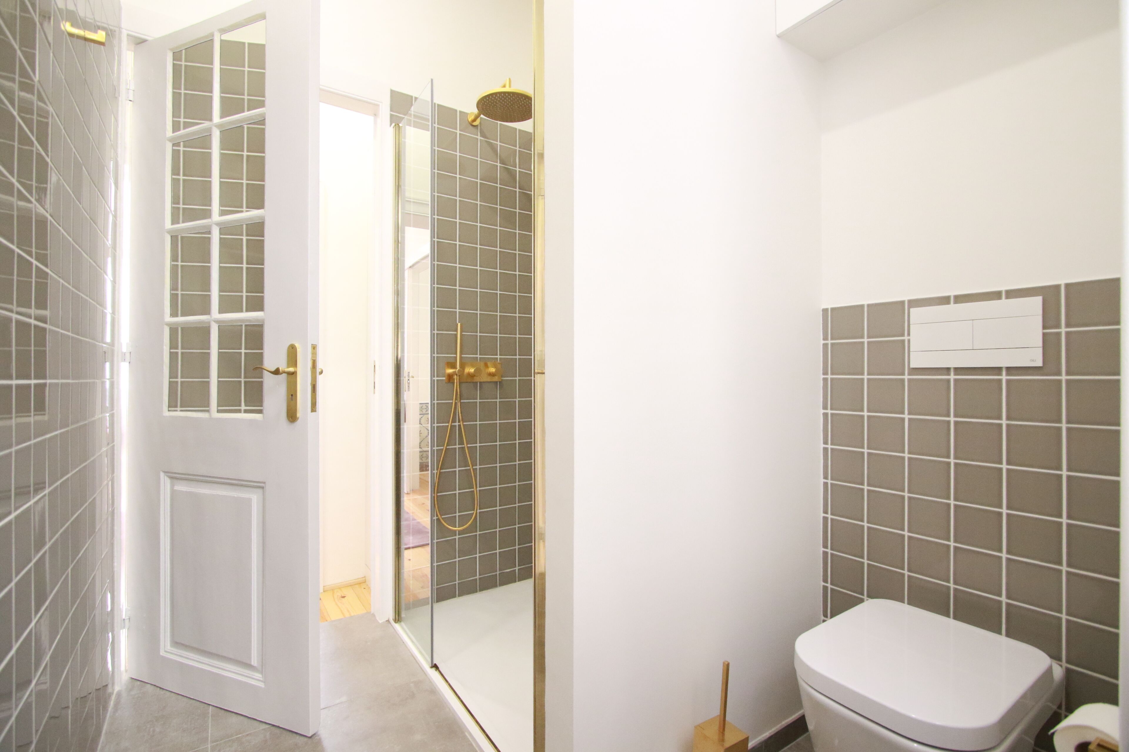 Casa de banho com chuveiro, sanita e porta de vidro para outro espaço.