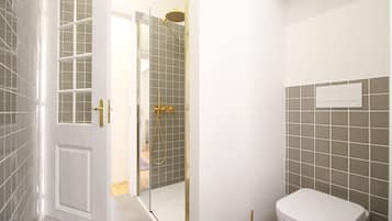 Casa de banho com chuveiro, sanita e porta de vidro para outro espaço.