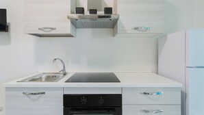 Cozinha moderna com pia de aço inoxidável, forno preto e armários brancos.