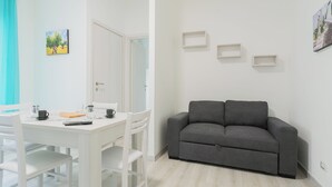 Uma sala de estar moderna com um sofá cinzento, uma mesa de jantar branca com cadeiras e uma porta que dá para outro cômodo.