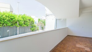 Uma varanda com piso de azulejos, paredes brancas e grade de metal.