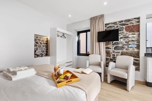 Quarto de hotel moderno com uma cama, duas poltronas, uma televisão, uma parede de pedra e um tabuleiro de café da manhã.