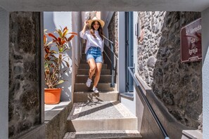 Uma mulher descendo uma escadaria de pedra, com um vaso de planta à esquerda e uma placa indicando o quinto andar de um edifício.
