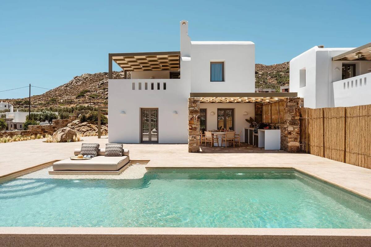 Uma villa moderna com piscina, área de refeições ao ar livre e paredes de pedra.