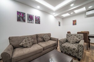 Uma sala de estar moderna com sofá, poltrona e mesa de centro. Três obras de arte emolduradas adornam a parede.
