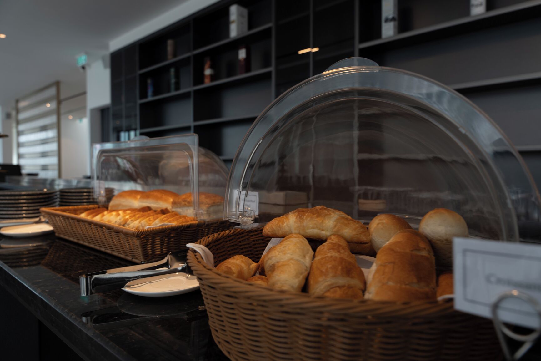 Uma área de buffet com cestos de pão e doces sob redomas.