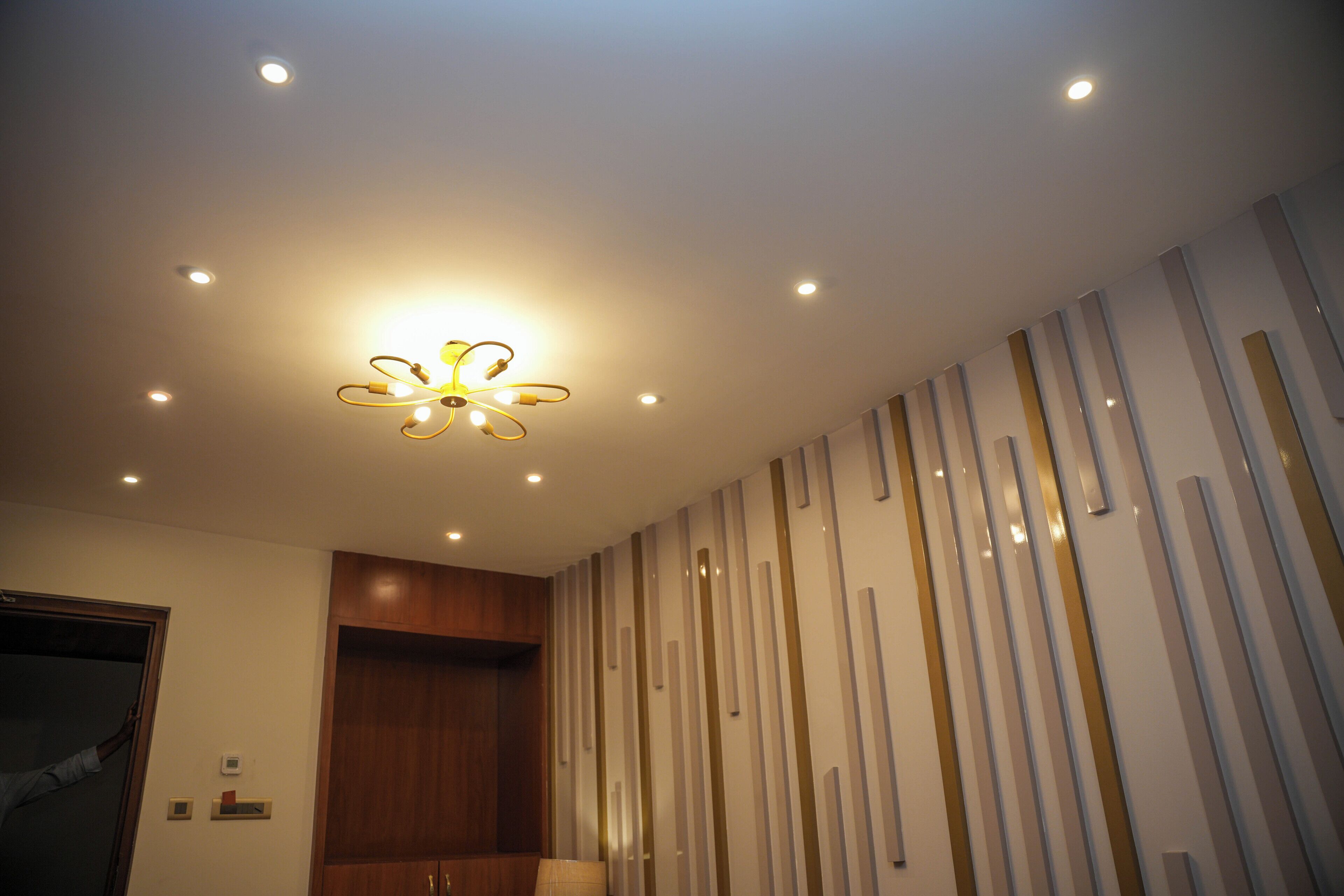 Um interior moderno com luminária no teto, iluminação embutida e parede com listras verticais.