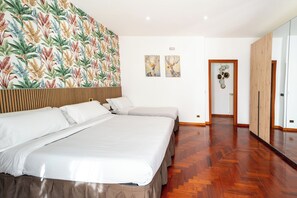 Quarto de hotel com duas camas, uma cabeceira de madeira, papel de parede floral e piso de madeira.