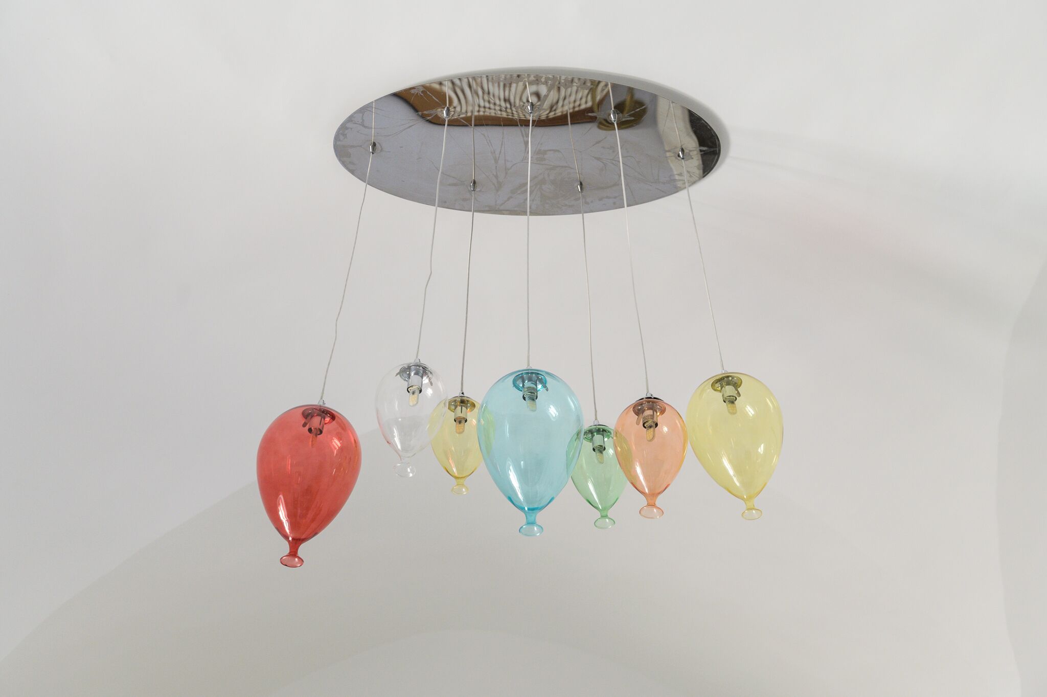Teto com superfície refletora circular e sete balões suspensos em várias cores.