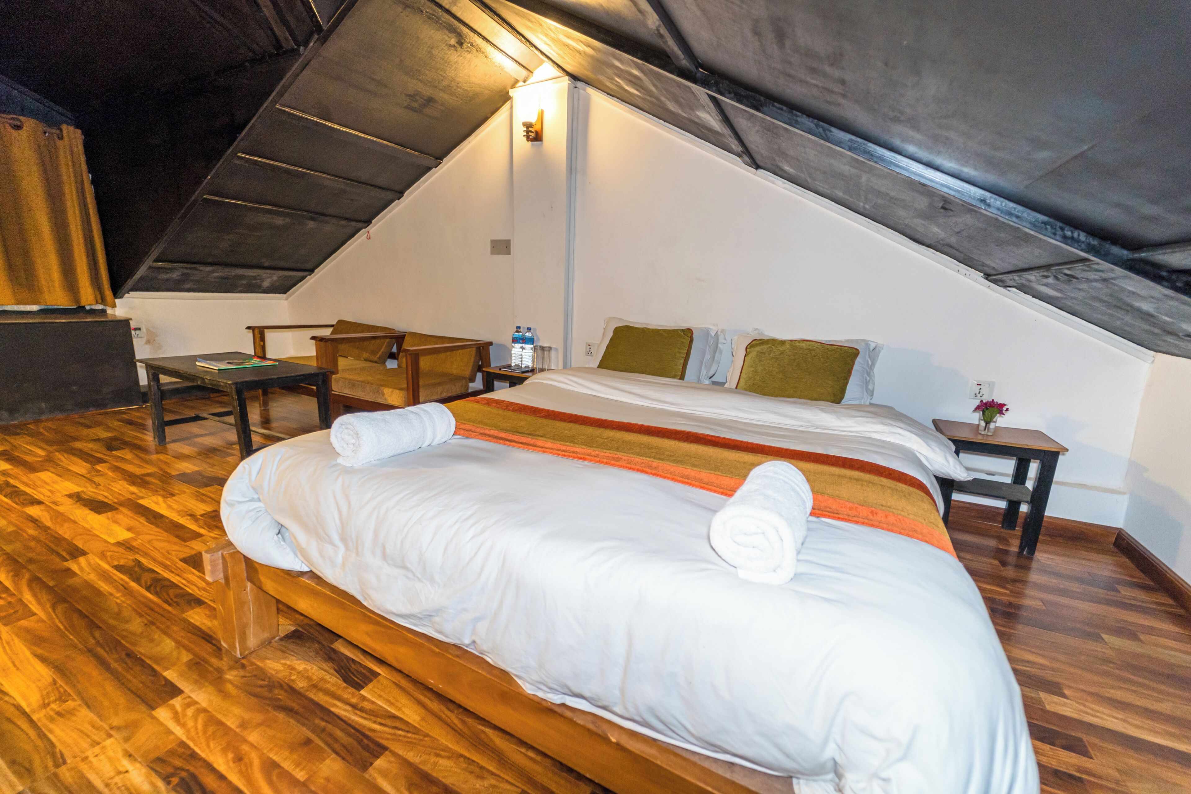 Quarto com cama de madeira, escrivaninha, cadeira e uma pequena mesa com uma garrafa de água.
