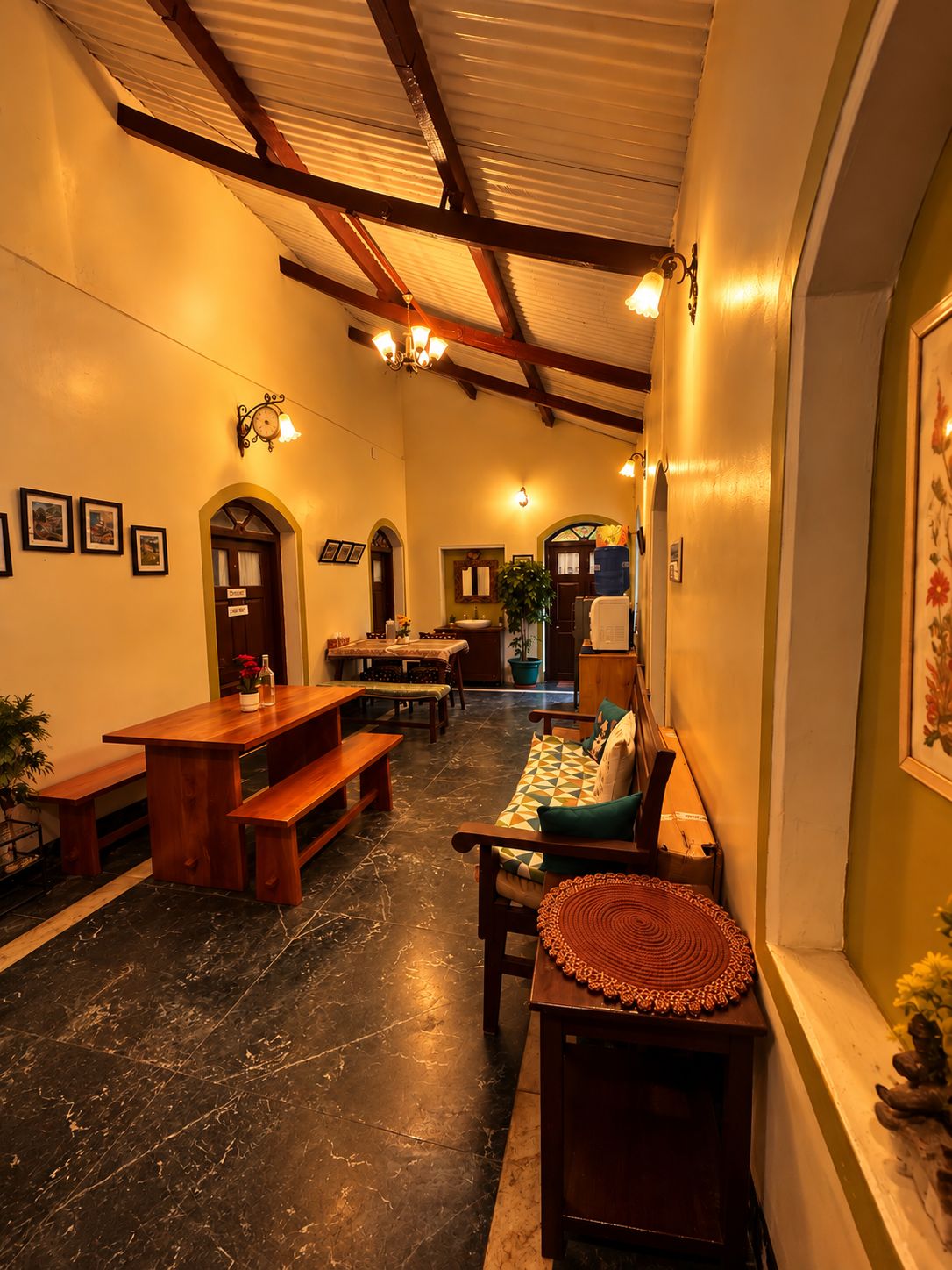 Um quarto amplo com teto alto, vigas de madeira, uma mesa de jantar comprida, bancos e um sofá estampado.