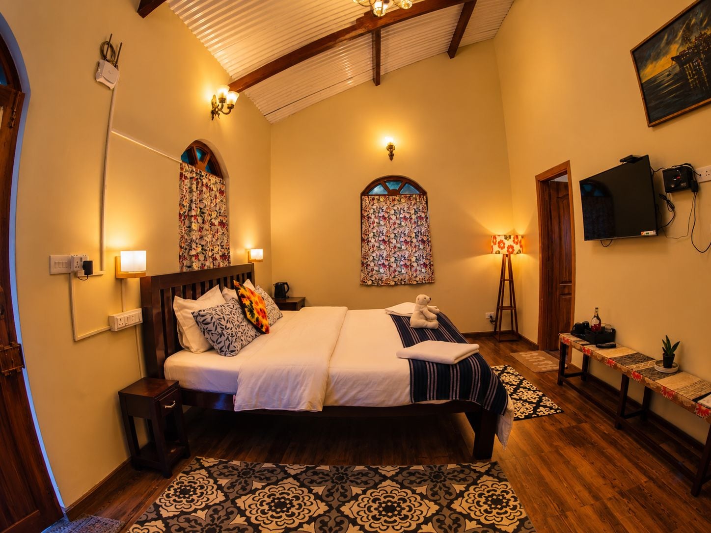 Quarto de hotel com uma cama grande, duas mesas de cabeceira, televisão e janela com cortinas.