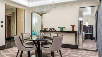 Quarto de hotel moderno com uma mesa de jantar redonda, quatro cadeiras, um candelabro, um espelho grande e vista para o corredor.