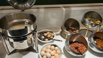Disposição de buffet com diversos pratos, incluindo uma panela grande, recipientes com ovos e recipientes com feijão.