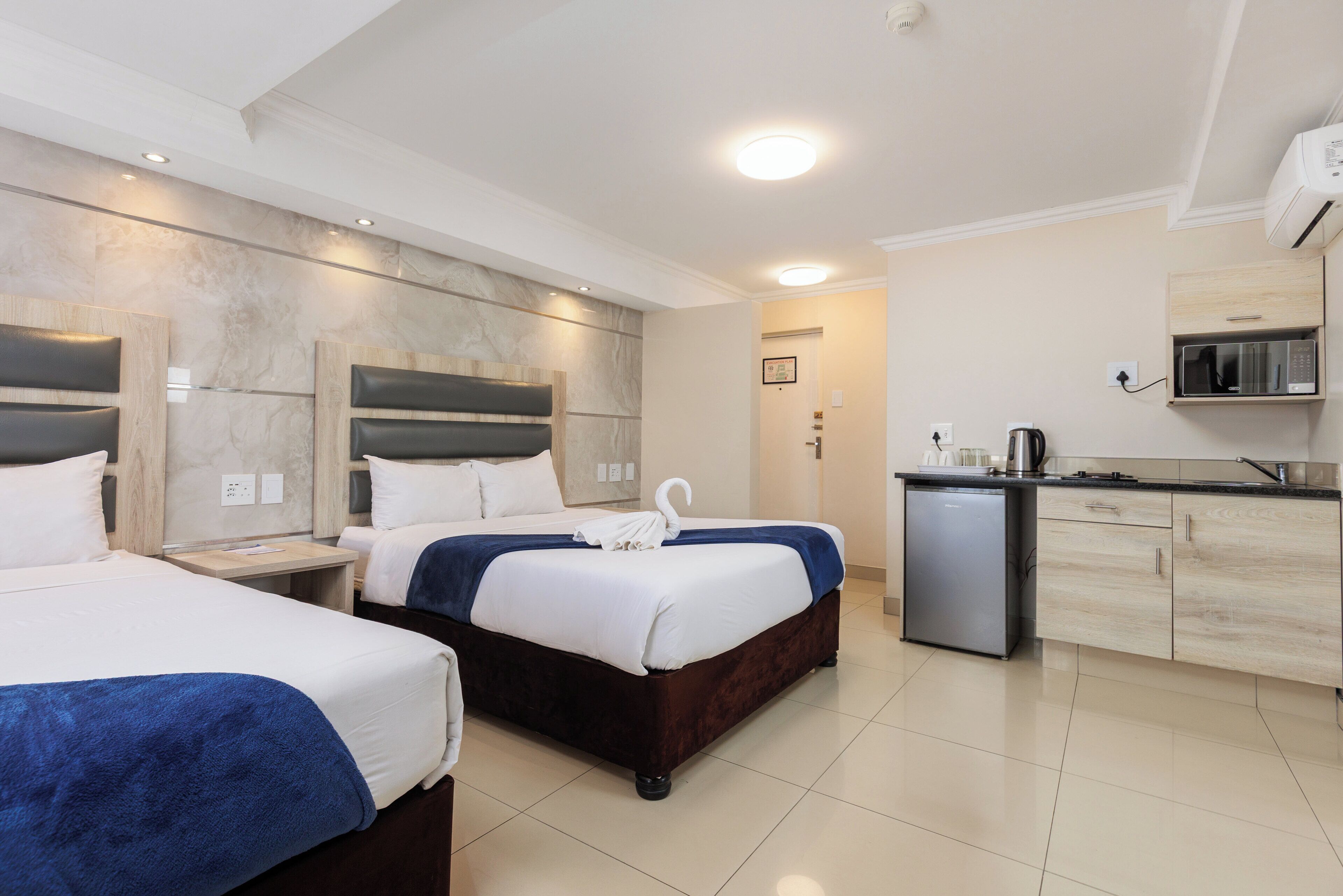 Quarto de hotel com duas camas, uma kitchenette e um banheiro.