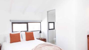 Quarto com uma cama, duas almofadas, uma mesinha de cabeceira com abajur e uma janela.