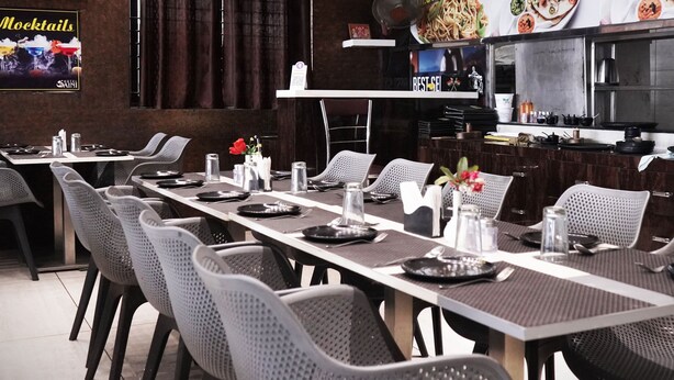 Restaurante com uma longa mesa de jantar posta com cadeiras, um quadro de menu e uma parede com um pôster.