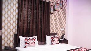 Quarto de hotel com cama, duas almofadas, mesa de cabeceira, telefone, abajur e um painel decorativo na parede.