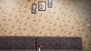 Quarto com sofá cinzento, mesa de centro de vidro e um vaso com flores vermelhas. Há três quadros na parede.