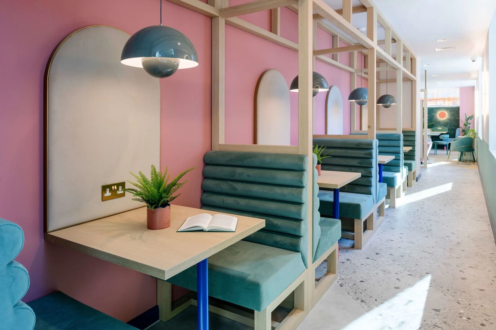 Um restaurante moderno com assentos cor de verde-água, paredes rosa e iluminação pendente.