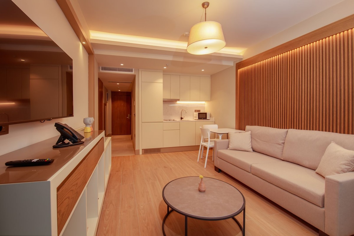 Uma sala de estar moderna com sofá, mesa de centro, televisão e área de cozinha.