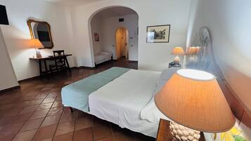 Quarto de hotel com cama, escrivaninha, cadeira, abajur e um quadro na parede.