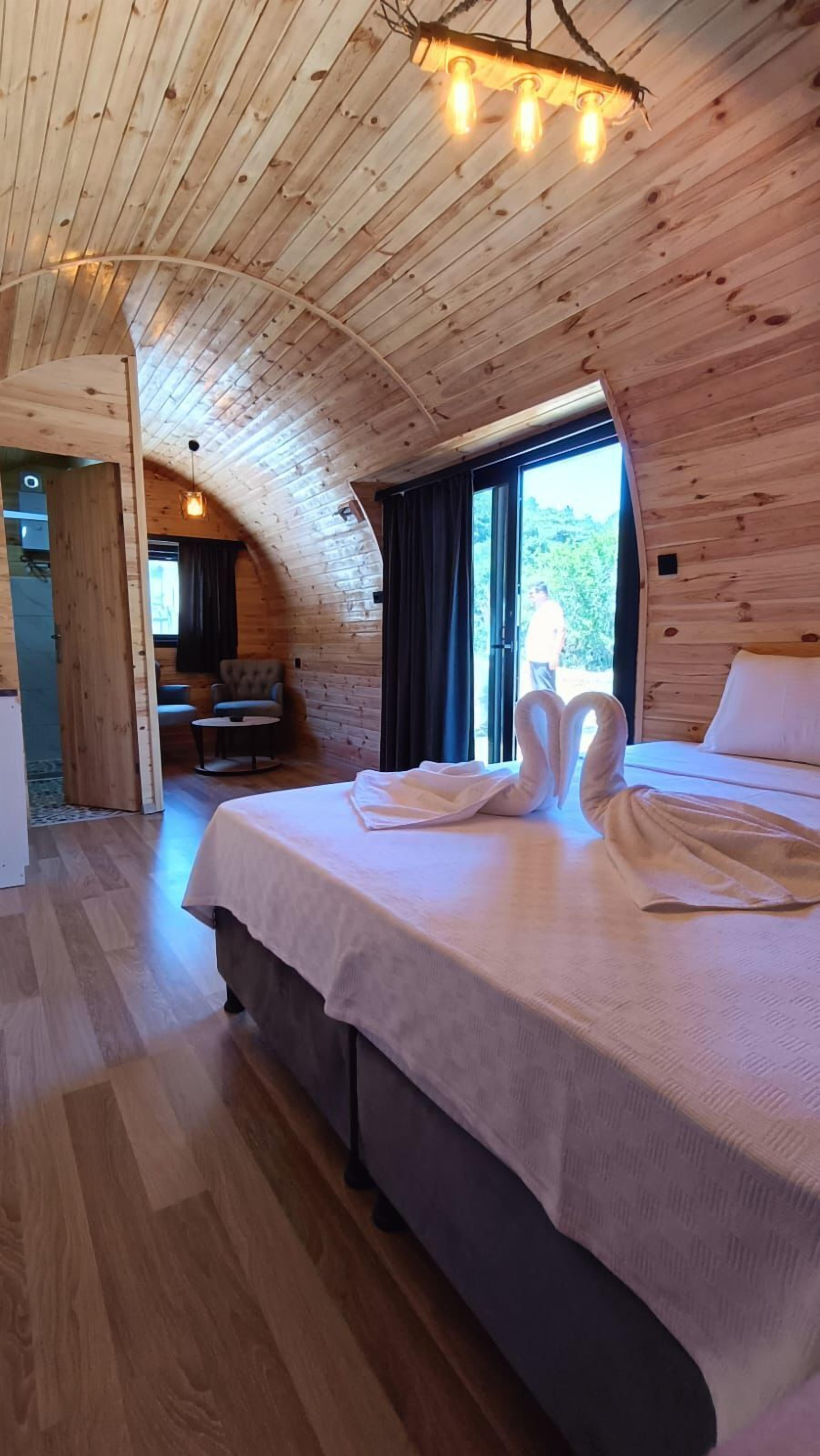 Quarto de cabana de madeira aconchegante, com cama, arranjo de toalhas em forma de cisne e janela com cortinas.