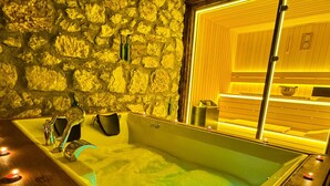 Uma área de spa com parede de pedra, banheira de madeira e velas.