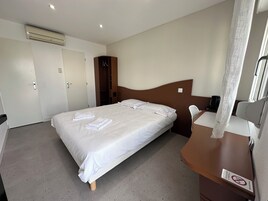 Quarto de hotel com cama, escrivaninha, cadeira, guarda-roupa e ar condicionado.