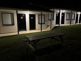Fileira de quartos de motel com portas numeradas, uma mesa de piquenique e uma área gramada.