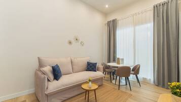 Uma sala de estar moderna com um sofá bege, uma mesinha redonda com um vaso, e um espaço de jantar com mesa e cadeiras.