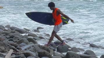 Uma pessoa caminhando numa praia rochosa com uma prancha de surf.