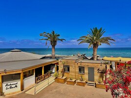Um restaurante à beira-mar com um espaço de terraço, palmeiras e vista para o mar.
