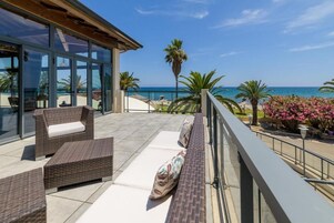 Varanda com mobiliário de vime, porta de vidro e vista para o mar.