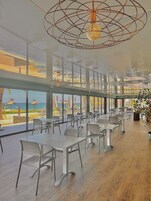 Uma sala de jantar espaçosa com janelas amplas, móveis modernos e vista para a praia.