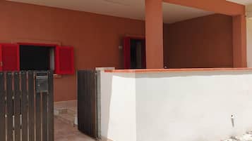 Um prédio residencial com varanda, portão fechado e uma porta vermelha.