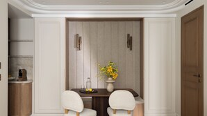 Uma área de refeições com mesa de madeira escura, duas cadeiras estofadas, um vaso com flores amarelas e um armário embutido com uma máquina de café.
