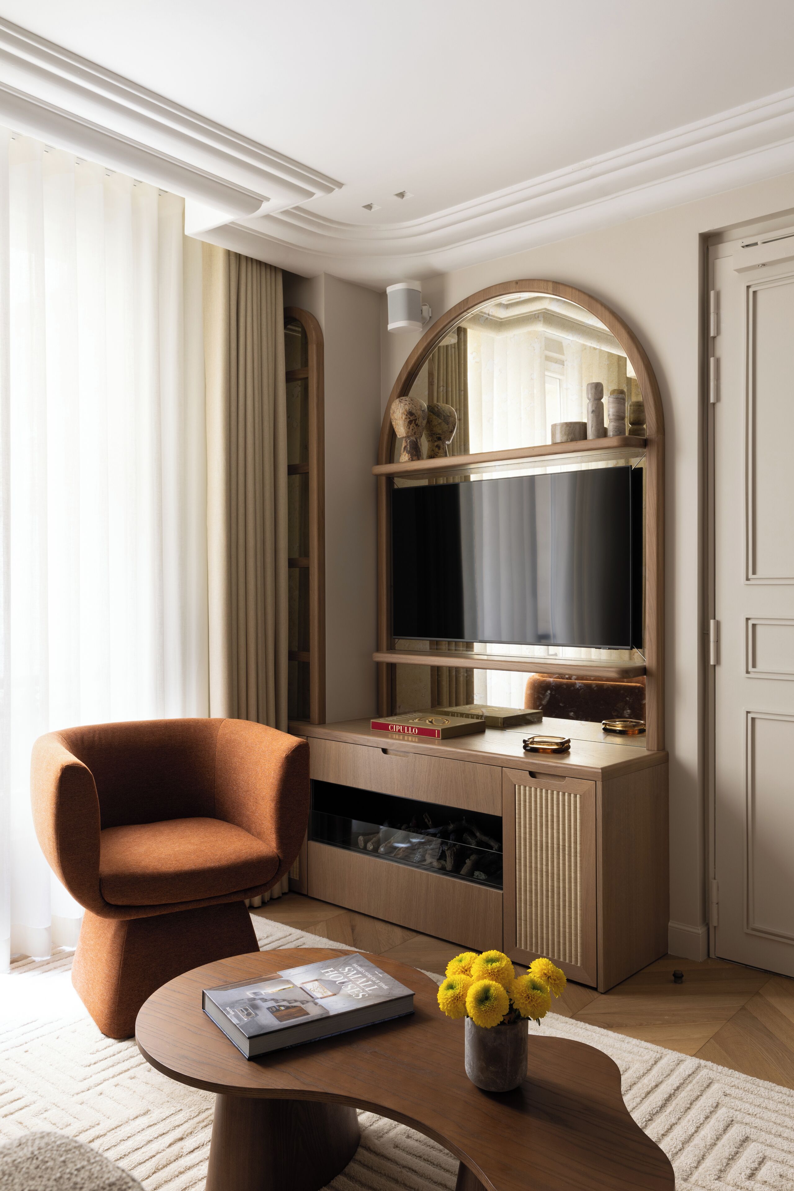 Uma sala de estar moderna com um sofá, uma mesa de centro com um livro e flores, uma televisão e uma estante de livros.