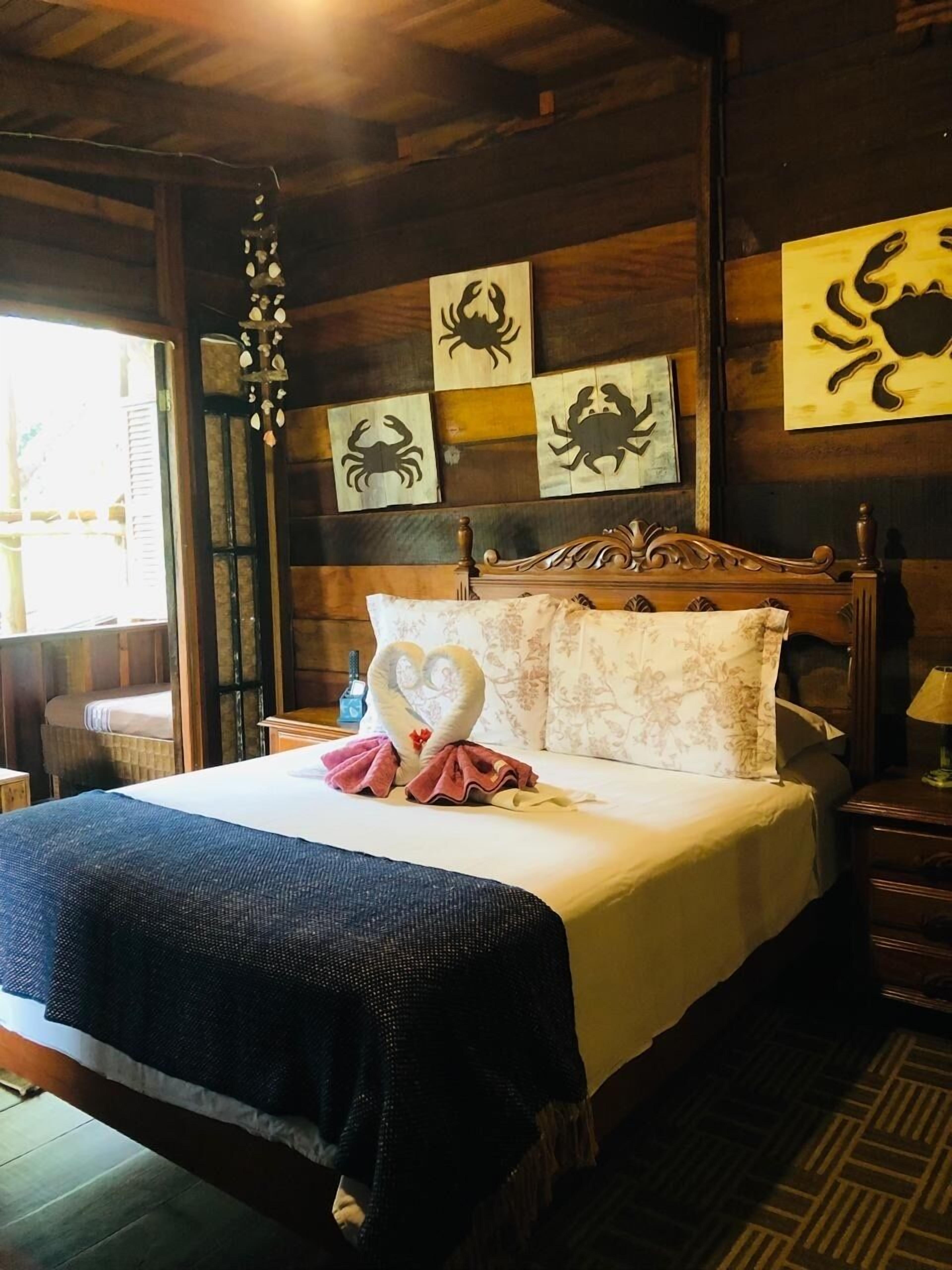 Um quarto de madeira com uma cama, luminária pendente e quadros de caranguejos.
