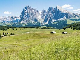 Paisagem montanhosa com céu claro, campos verdes e edifícios espalhados.