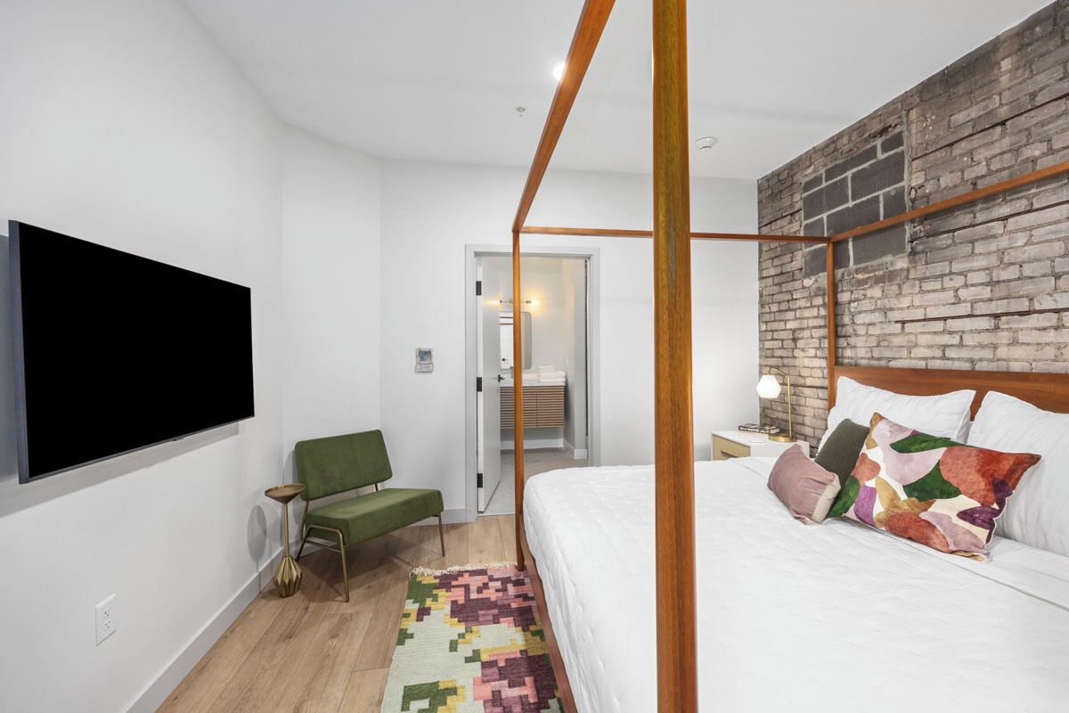 Quarto moderno com uma cama grande, televisão fixada na parede, uma poltrona verde e um tapete estampado.