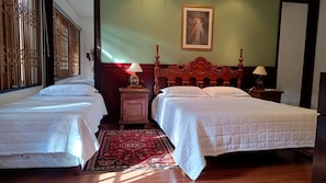 Quarto de hotel com duas camas de solteiro, cabeceira de madeira, tapete com padrão vermelho e um quadro na parede.