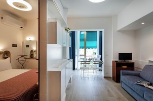 Quarto de hotel moderno com cama, área de estar com sofá, mesa de jantar com cadeiras, televisão e varanda com vista.