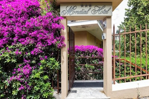 A entrada do Hotel Mondial, com uma placa sobre a porta, cercada por vibrantes bougainvilleas cor-de-rosa.