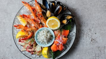 Prato de frutos do mar com camarões, mexilhões, salmão e polvo, acompanhado de fatias de limão e uma pequena tigela de arroz.