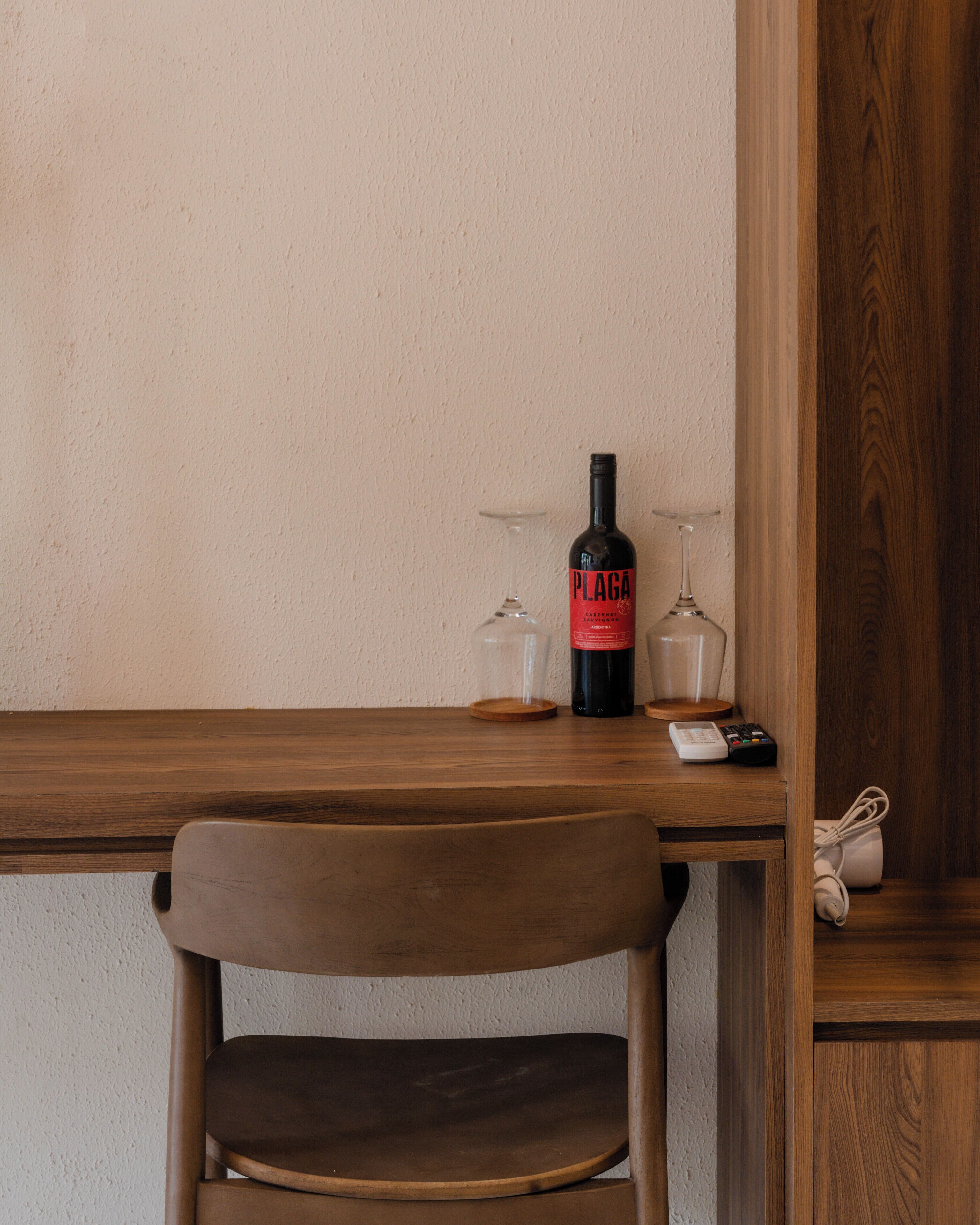 Uma mesa de madeira com uma garrafa de vinho Plaga, dois copos de vinho e um controle remoto.